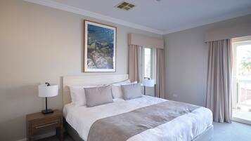 Quarto bem arrumado com uma cama grande, abajures, uma obra de arte emoldurada na parede e uma janela com cortinas.