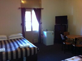 Quarto de hotel com cama, escrivaninha, cadeira, televisão e janela com cortinas.