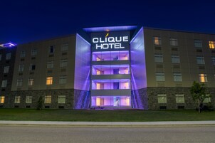 Um hotel com vários andares, com uma placa chamativa 'CLIQUE HOTEL', apresentando um design arquitetônico moderno com telhado plano e fachada de pedra e vidro.