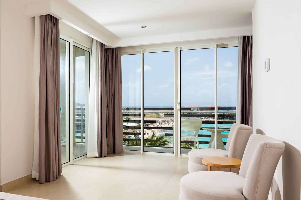 Quarto de hotel moderno com uma varanda grande, vista para a piscina e uma área de estar confortável.