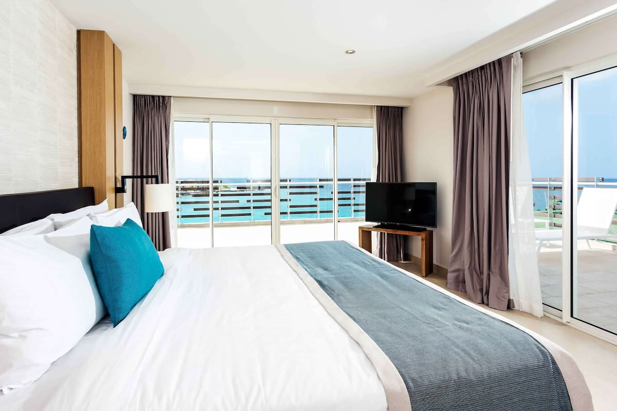 Quarto de hotel com cama grande, televisão e varanda vista para o mar.