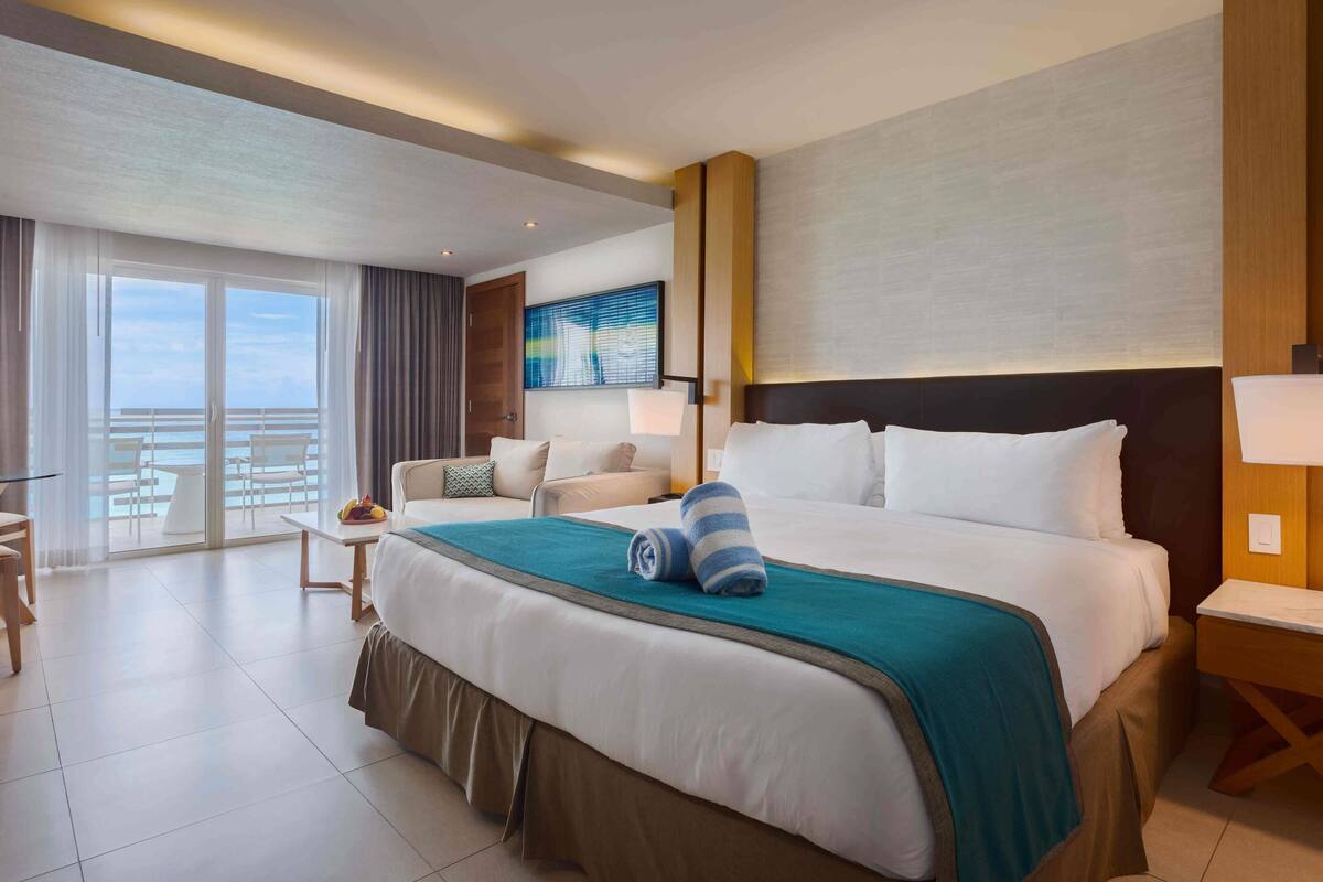 Quarto de hotel com cama grande, mesa de trabalho, cadeira, varanda com vista e design moderno.