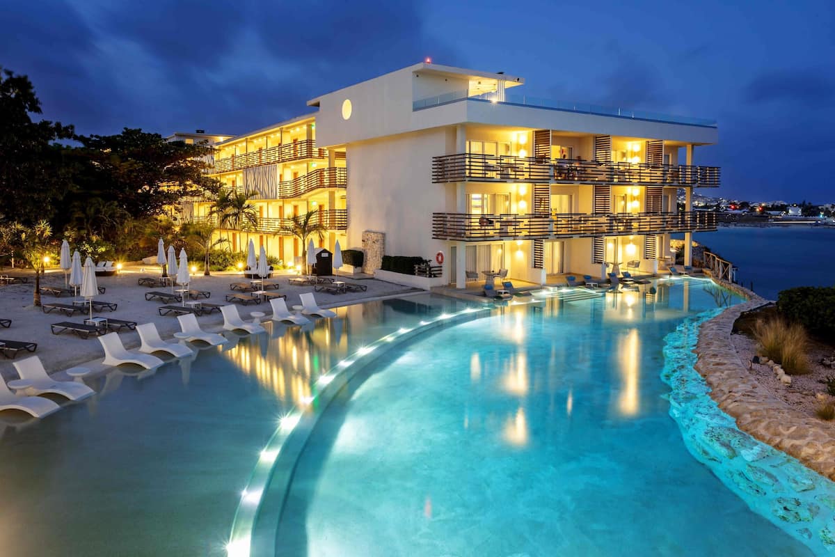 Um hotel moderno com uma grande piscina infinita, área de estar ao ar livre e vista para o mar.