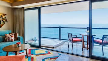 Uma varanda com vista para o mar, um sofá, uma mesa de centro e uma mesa pequena com cadeiras.