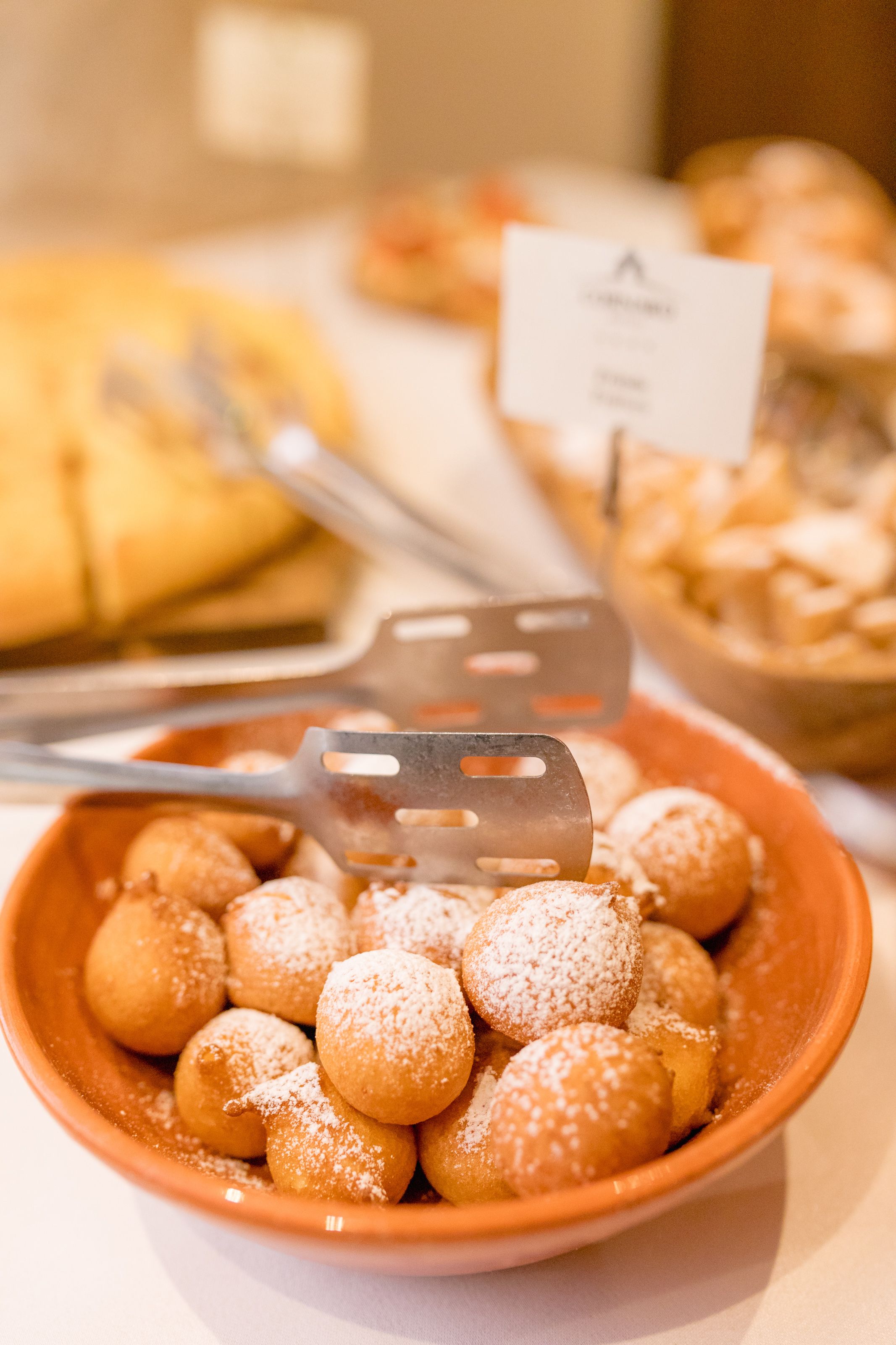Uma tigela de doces redondos e em pó, com uma colher de servir.