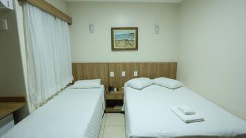 Quarto de hotel com duas camas de solteiro, cabeceira de madeira, mesa de cabeceira com telefone e um quadro na parede.