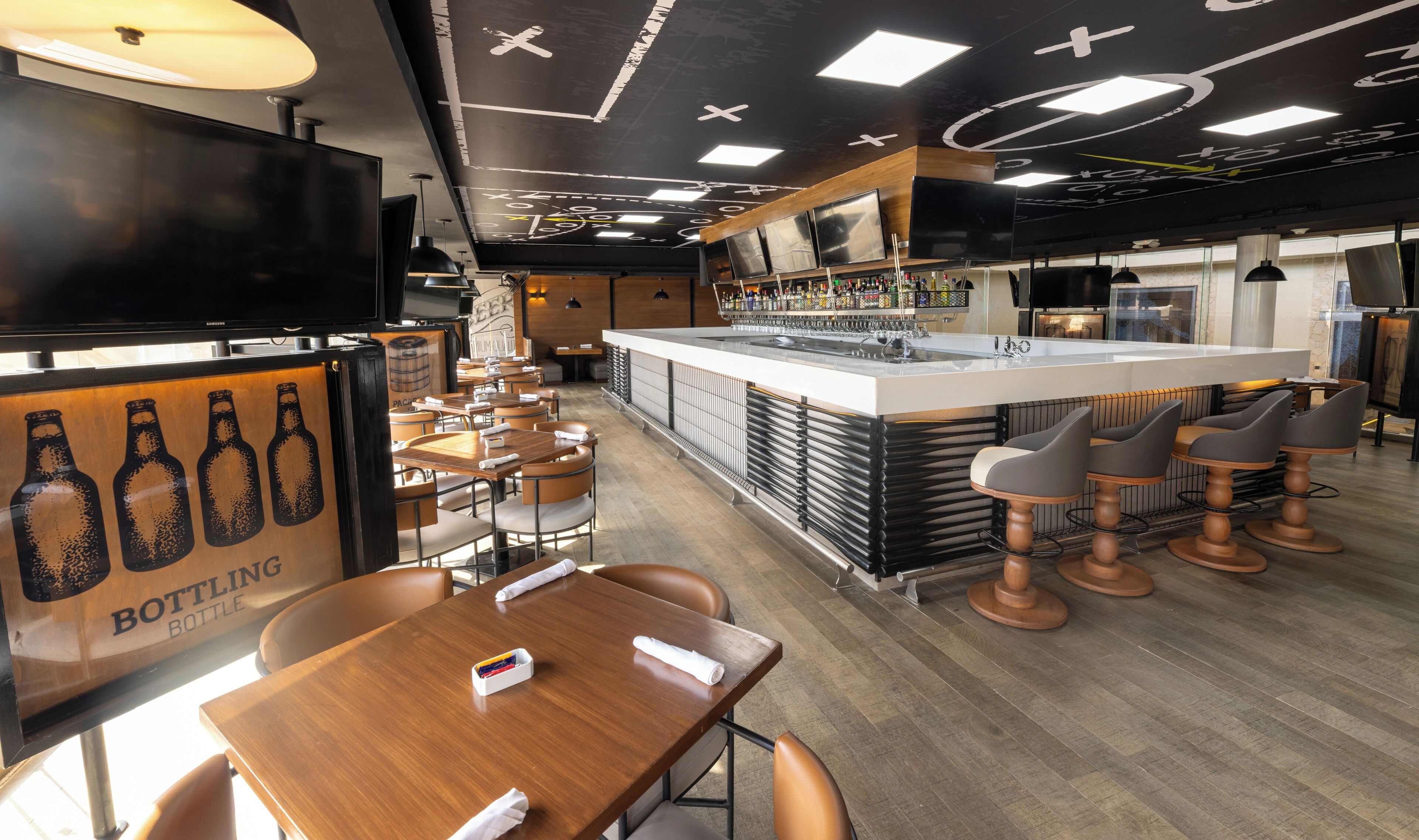 Uma área de bar com mesas e bancos de madeira, um balcão e uma exposição de garrafas de cerveja.