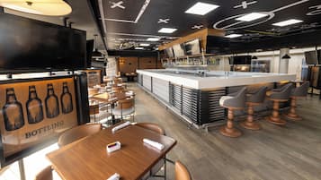 Uma área de bar com mesas e bancos de madeira, um balcão e uma exposição de garrafas de cerveja.