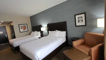 Quarto de hotel com duas camas de solteiro, um sofá de couro marrom, uma mesa pequena e uma mesinha de cabeceira com abajur.