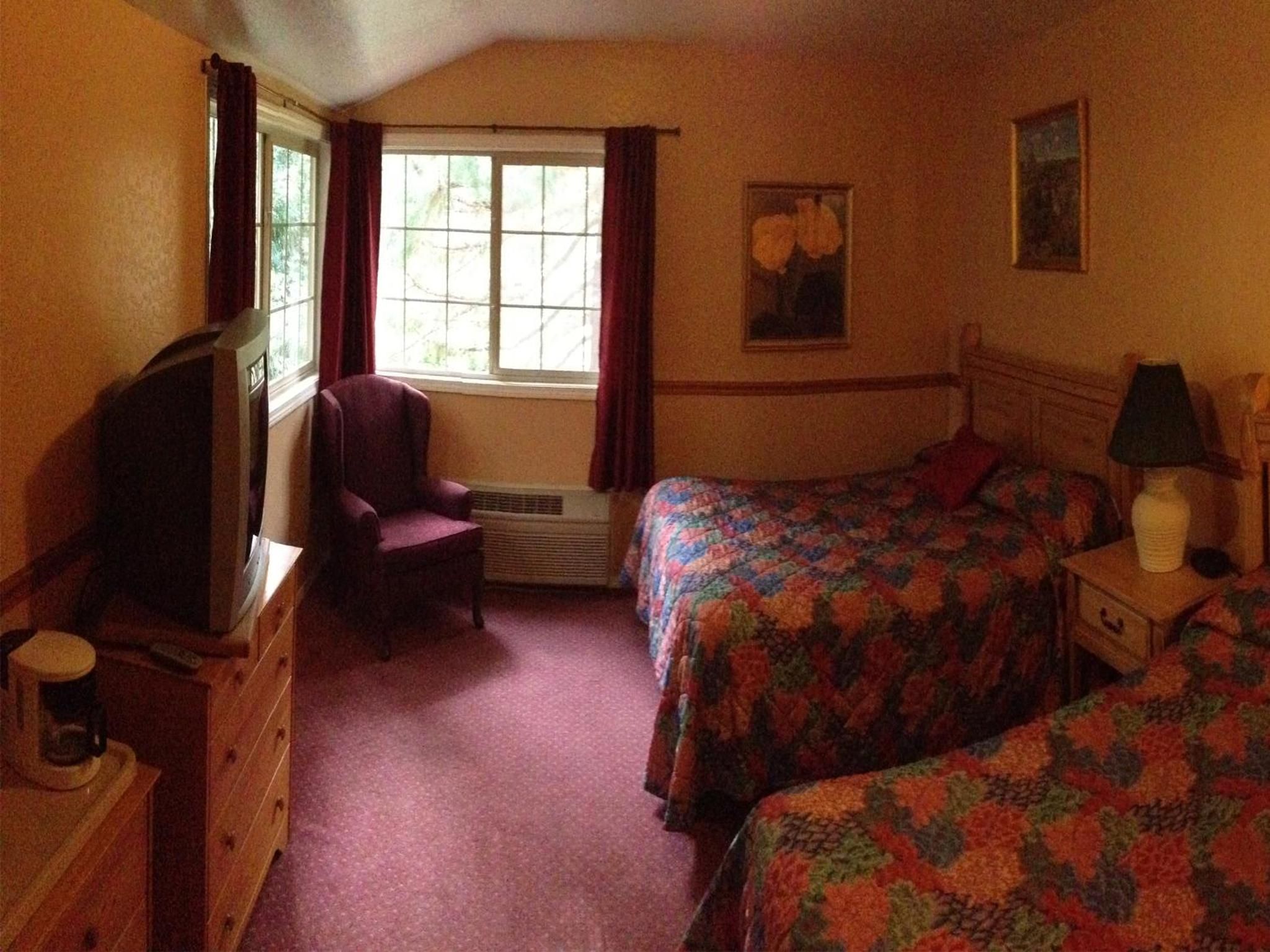 Quarto com duas camas, uma cadeira, televisão e janela com cortinas.