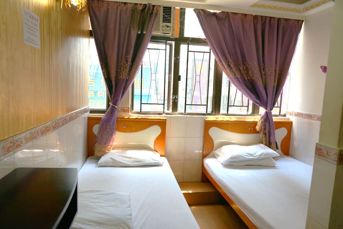 Quarto com duas camas, uma janela com cortinas roxas e cabeceira de madeira.