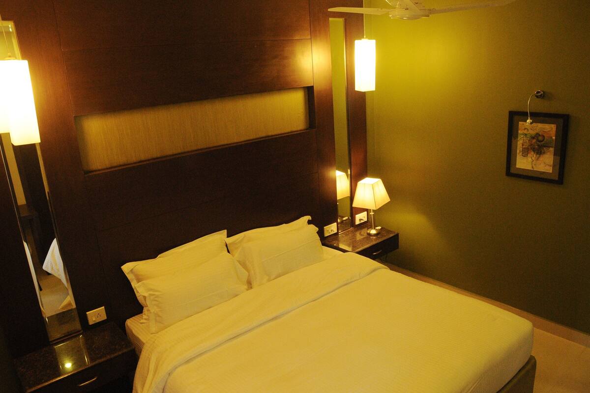 Cama bem arrumada com lençóis brancos, cabeceira de madeira e duas luminárias de cabeceira em um criado-mudo.