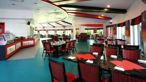 Um restaurante com mobiliário vermelho e preto, um balcão com vitrine e grandes janelas.
