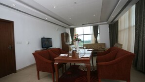 Uma sala de jantar com uma mesa de madeira, duas cadeiras vermelhas, um vaso com flores e um sofá ao fundo.