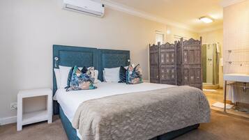 Quarto com cama, mesa de cabeceira, aparelho de ar condicionado, chuveiro e banheiro com pia.