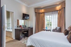 Quarto de hotel com uma cama grande, uma escrivaninha com espelho, televisão e vista para o exterior pela janela.