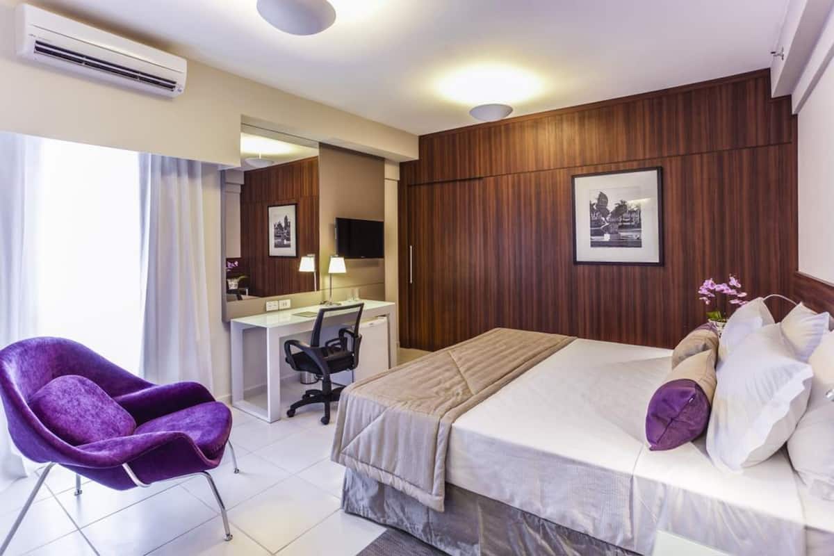 Quarto de hotel com uma cama, uma mesa, uma cadeira e uma televisão.
