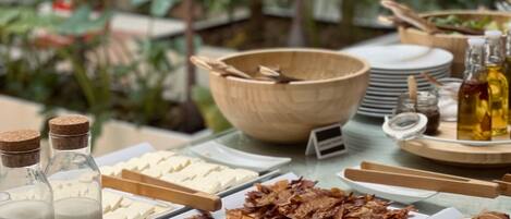 Uma mesa de buffet com diversos alimentos e etiquetas, em um ambiente de jardim.