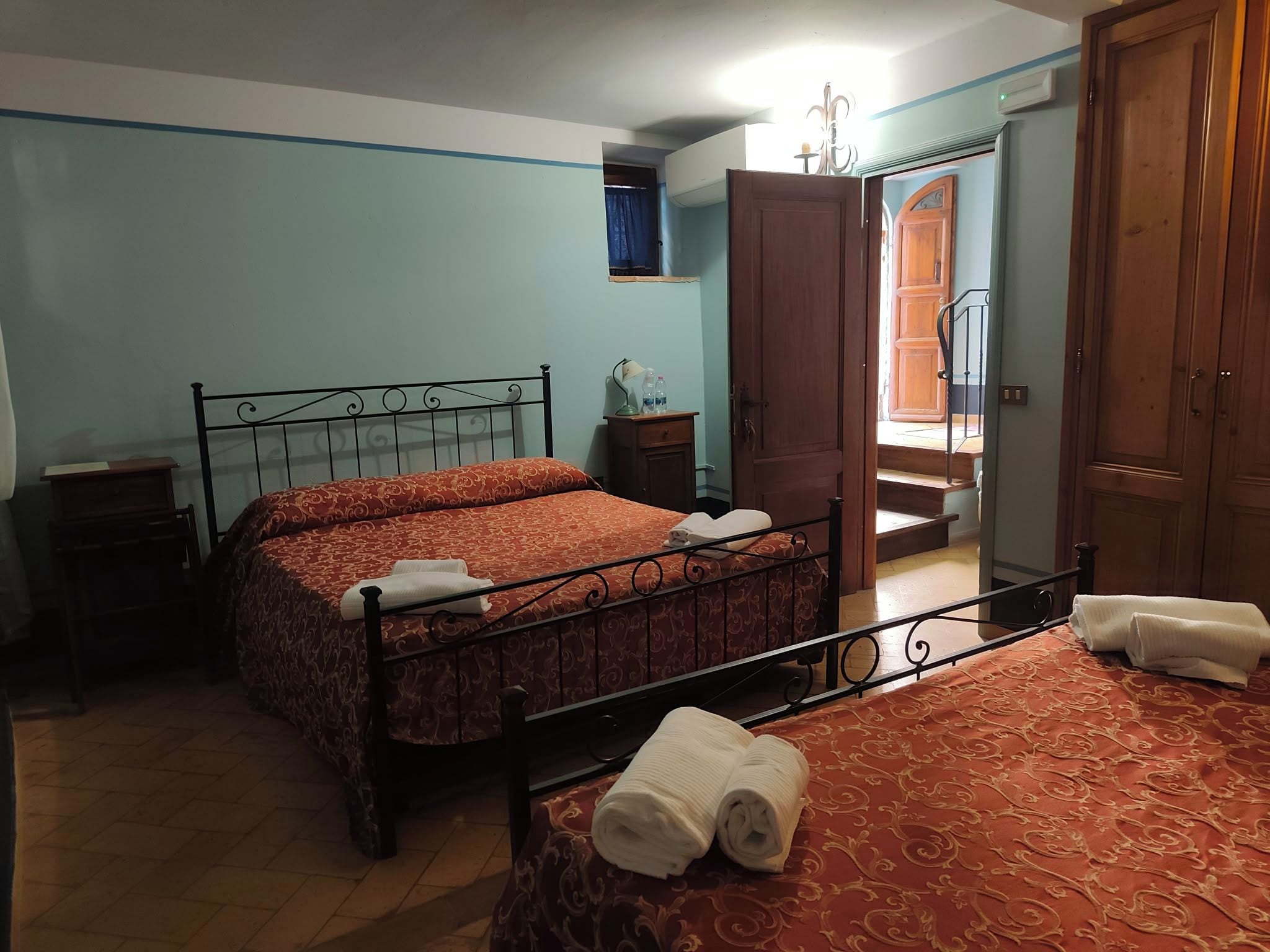 Quarto com uma cama de casal, mesa de cabeceira, guarda-roupa e uma porta que dá para outro cômodo.