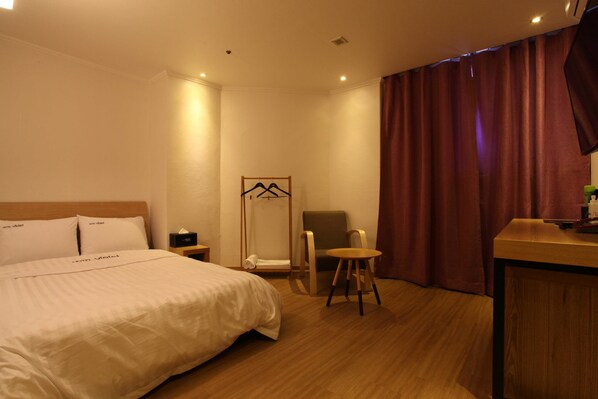 Quarto de hotel com uma cama, uma cadeira, uma escrivaninha e um espelho.
