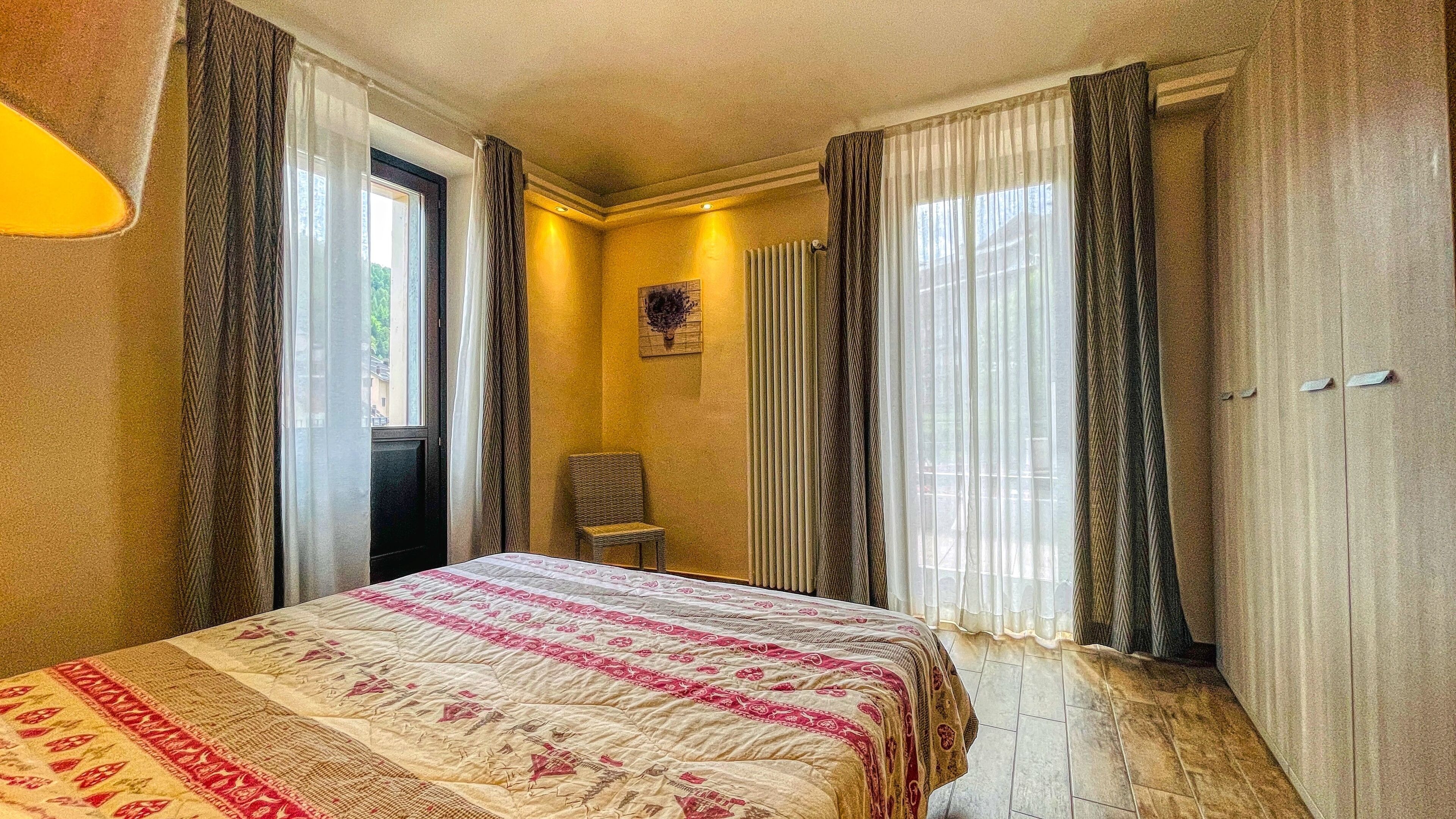 Quarto com cama, cadeira, radiador e cortinas.