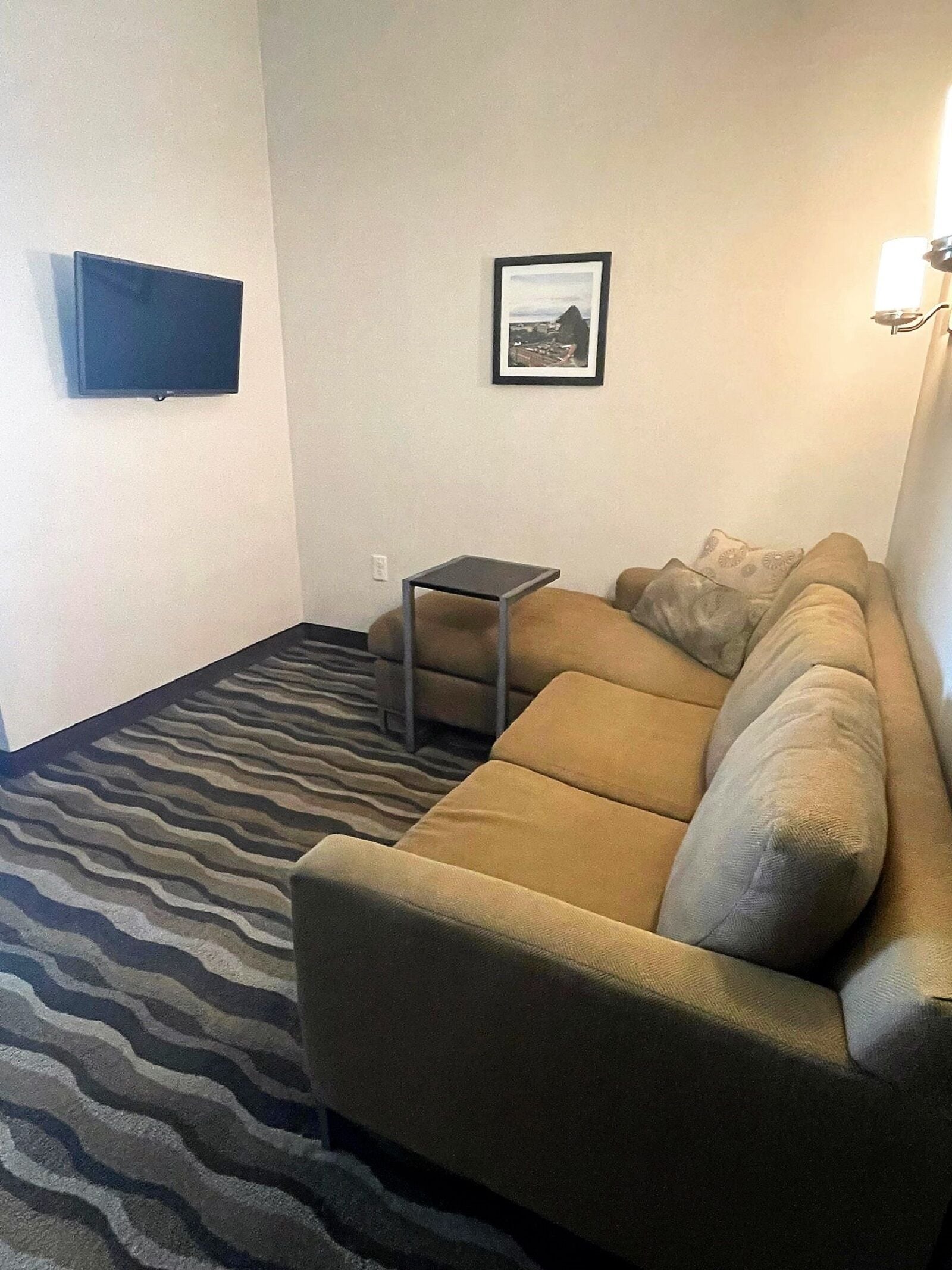 Sala de estar com sofá bege, uma mesinha, televisão de tela plana na parede e um quadro emoldurado.
