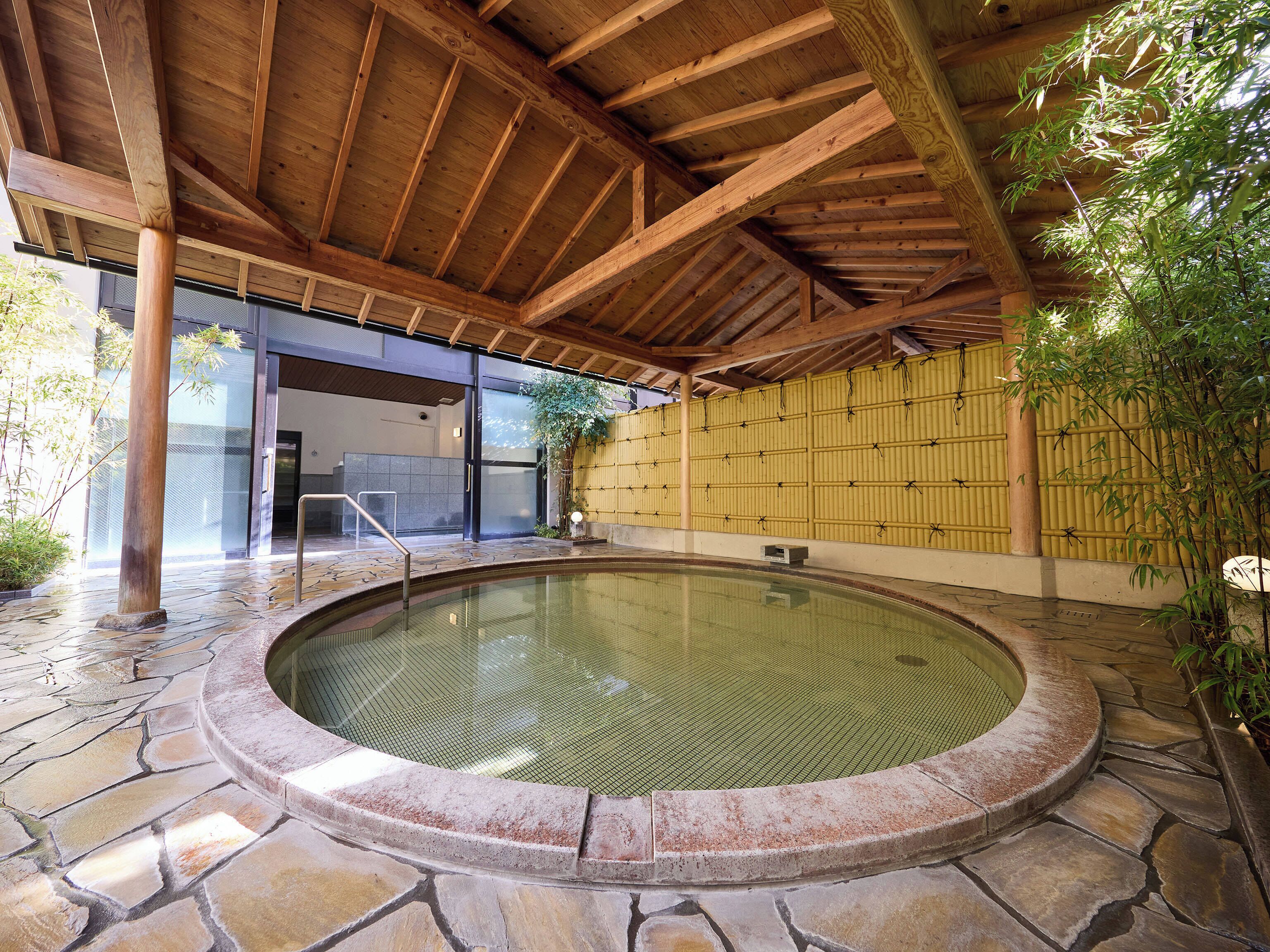Uma área de piscina com piso de lajes de pedra, teto de madeira e parede de bambu.