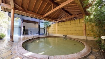 Uma área de piscina com piso de lajes de pedra, teto de madeira e parede de bambu.