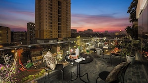 Terraço no telhado com área de refeições, cadeiras e plantas em vasos.