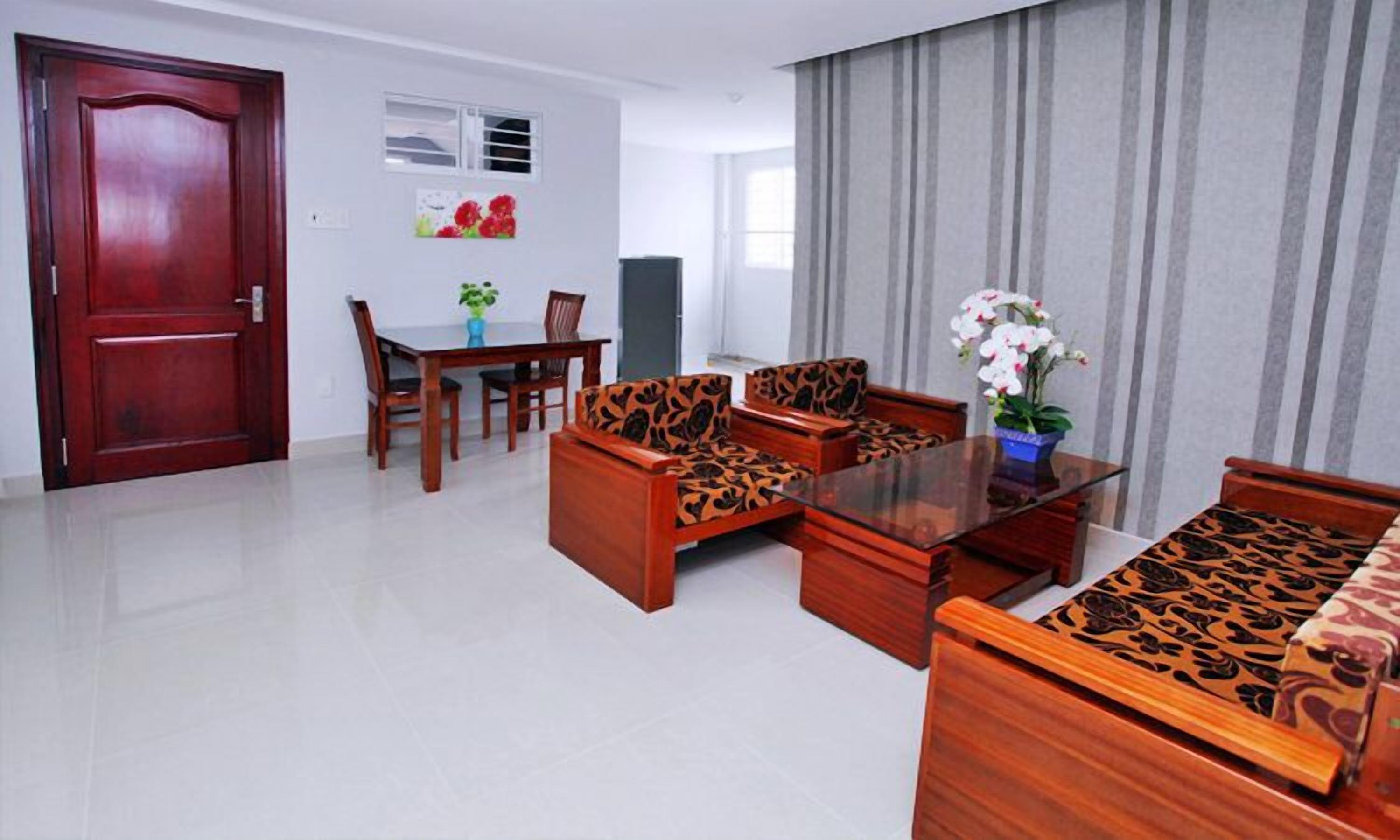 Uma sala de estar com sofá, poltrona e mesa de centro. Há também uma mesa de jantar com cadeiras e uma TV.