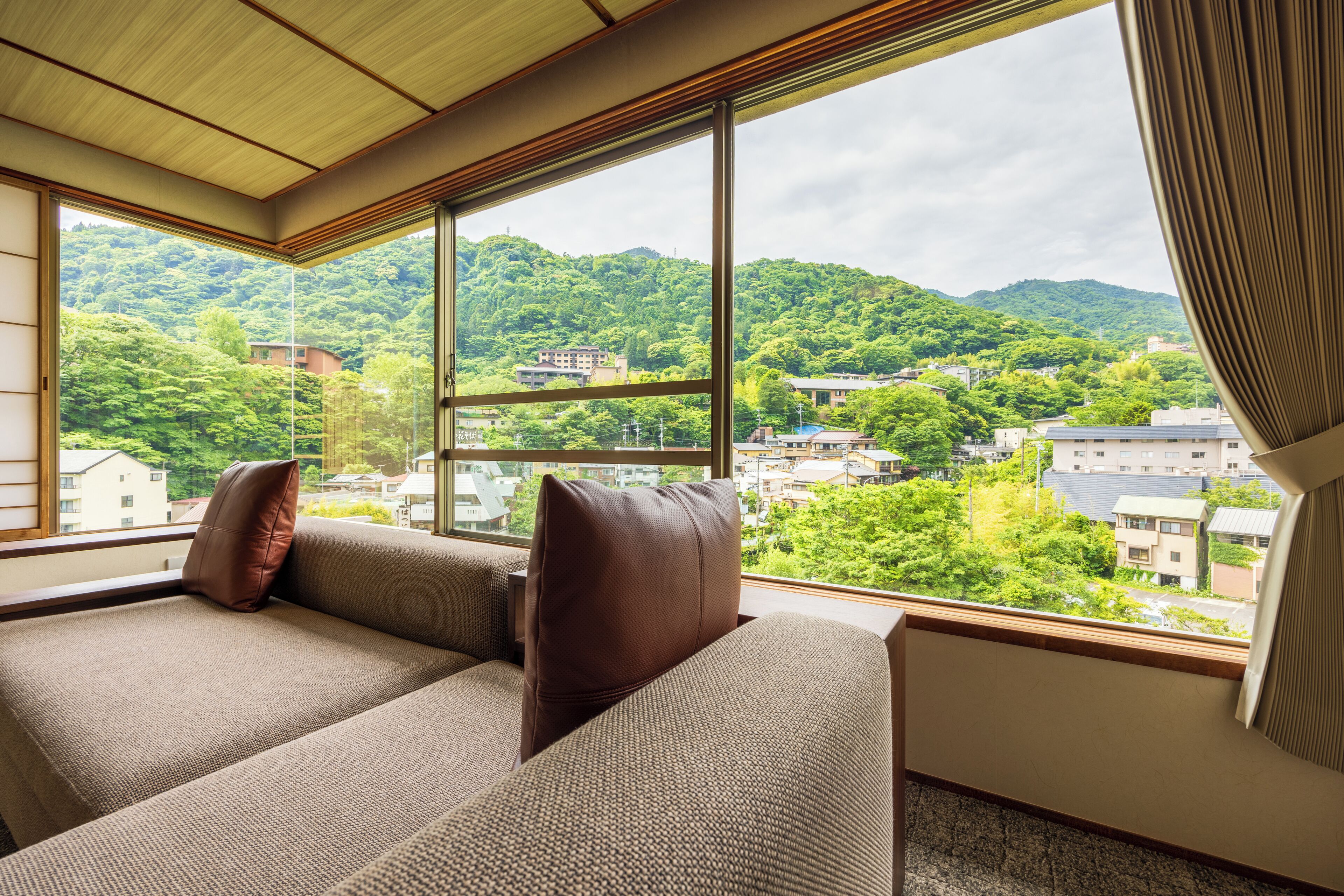 Quarto com uma janela ampla que oferece vista para uma encosta verde e edifícios.