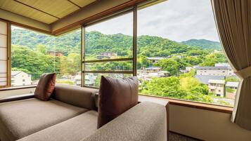 Quarto com uma janela ampla que oferece vista para uma encosta verde e edifícios.