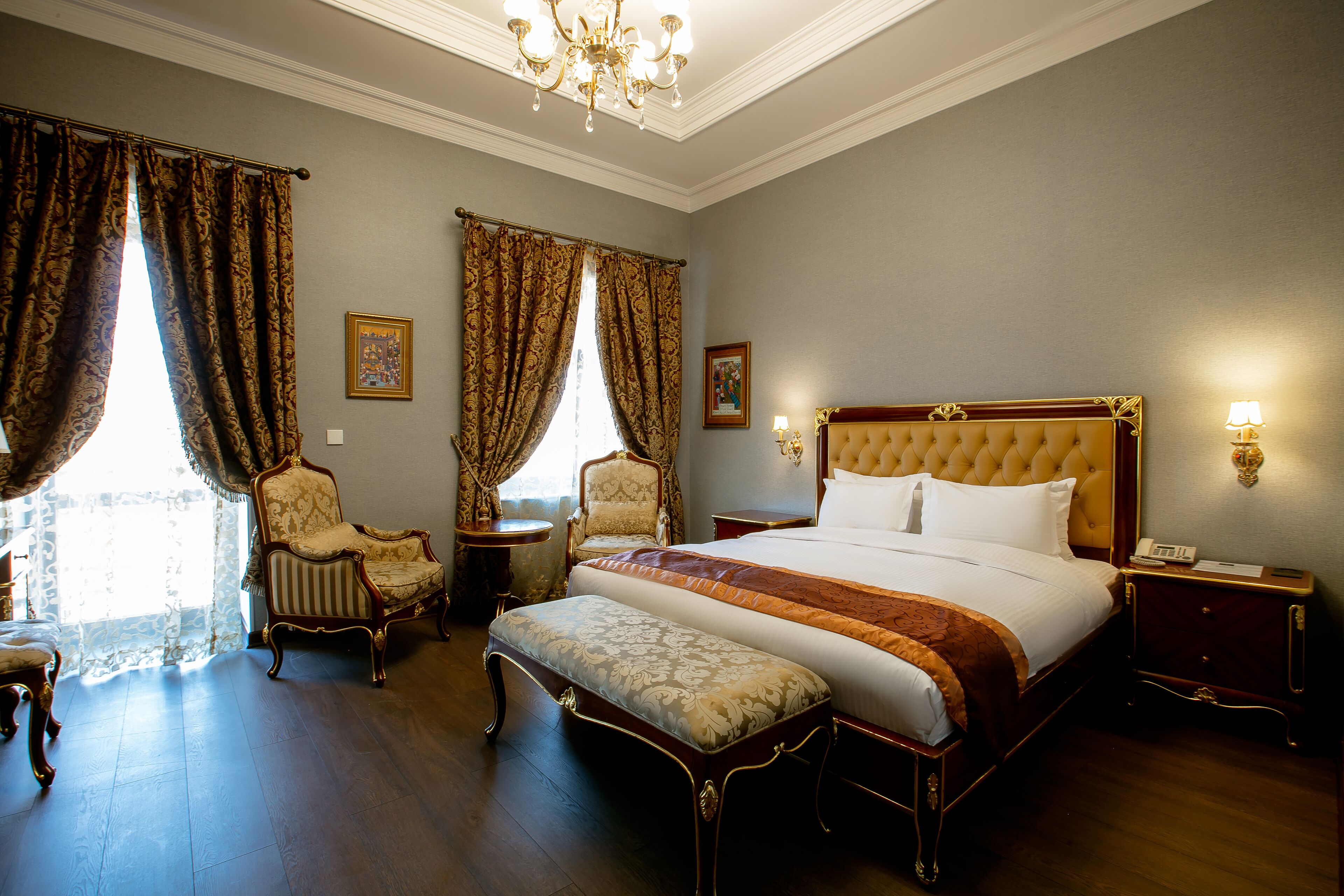 Quarto de hotel clássico com uma cama grande, duas poltronas, um banco e um candelabro.