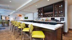 Uma área de bar com um balcão comprido, banquetas e uma televisão sobre o balcão.