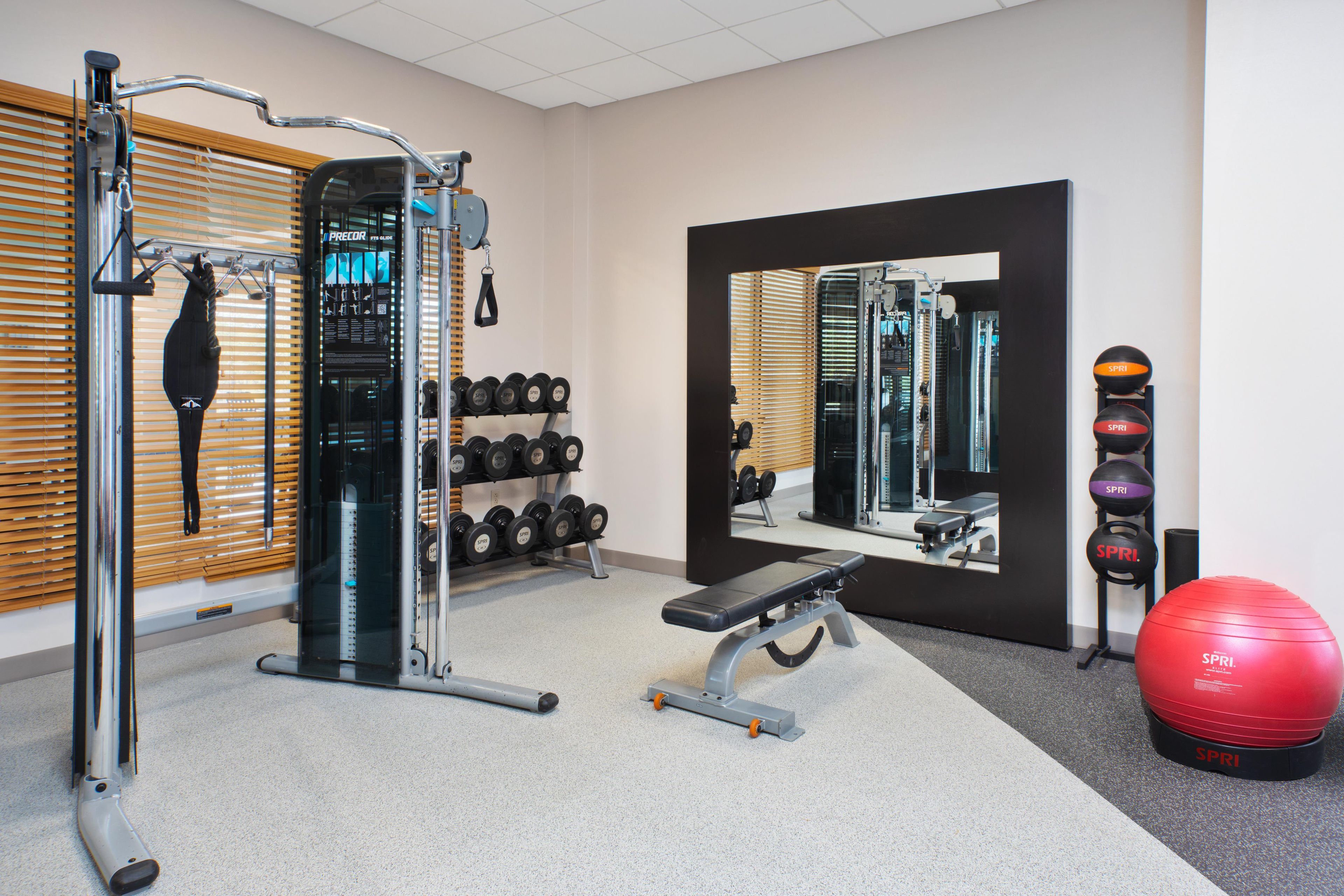 Uma academia com equipamentos de exercícios, um banco, uma bola vermelha para exercícios e um espelho.