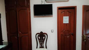 Quarto com guarda-roupa de madeira, televisão na parede, uma cadeira de madeira e porta com aviso.