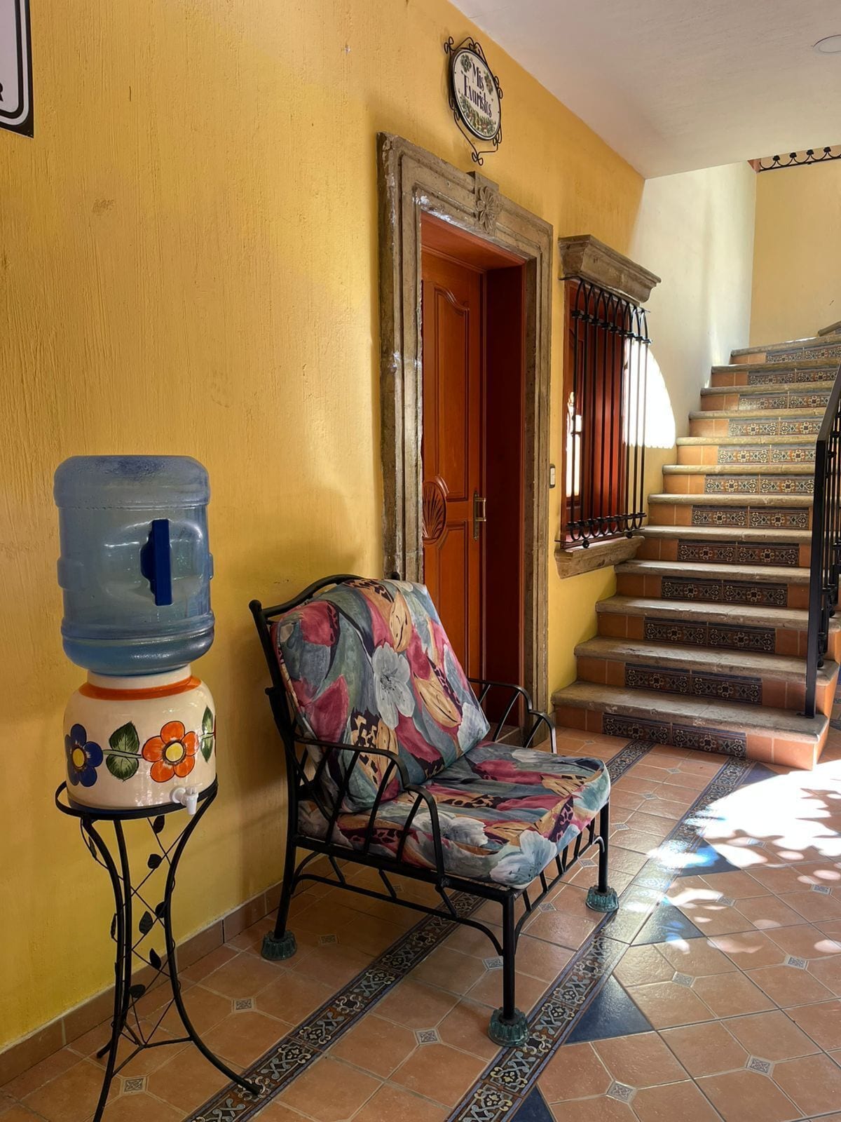 Quarto com um dispensador de água, uma cadeira de padrão floral, uma escada e uma porta.