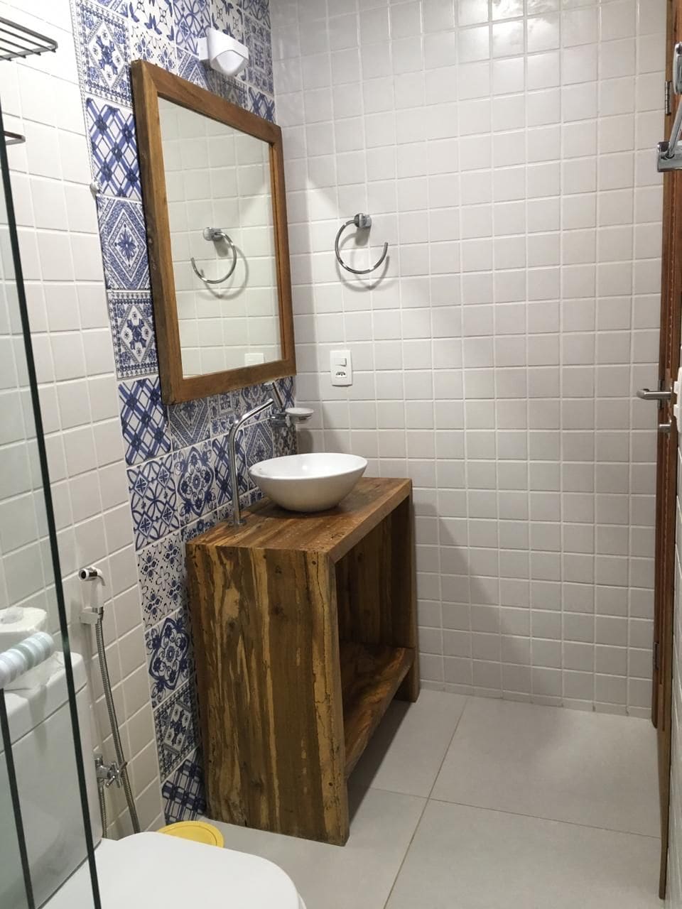 Casa de banho com toucador de madeira, uma pia branca, espelho e zona de duche.