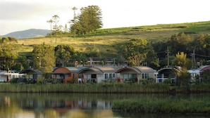 Fileira de casas móveis à beira de um lago tranquilo, com uma colina gramada ao fundo.