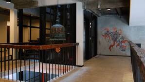 Um espaço interno amplo, com guarda-corpo de madeira, luminária pendente e um painel decorativo na parede.