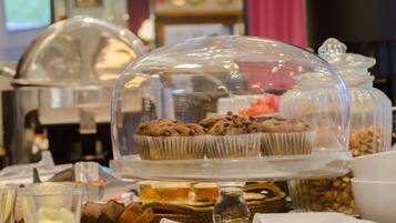 Buffet com diversos alimentos, incluindo muffins e doces sob cúpulas de vidro.