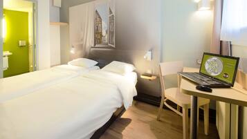 Quarto de hotel com cama, escrivaninha, um laptop e uma cadeira.