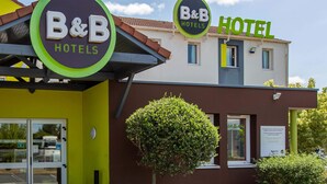 Um hotel tipo B&B com fachada verde e branca, entrada visível e uma placa.