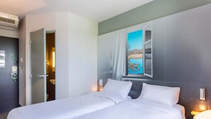 Quarto de hotel com uma cama grande, um banheiro visível por uma porta aberta e um quadro de uma paisagem na parede.