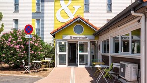 A building with a yellow facade and a large "&" sign, featuring a 'Bienvenue' sign at the entrance.
