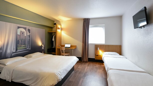 Quarto de hotel com duas camas, uma escrivaninha, uma cadeira, televisão e janela com cortinas.
