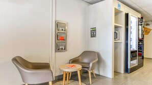 Quarto de hotel com minibar, área de estar com duas cadeiras e uma mesa pequena, e termostato fixado na parede.