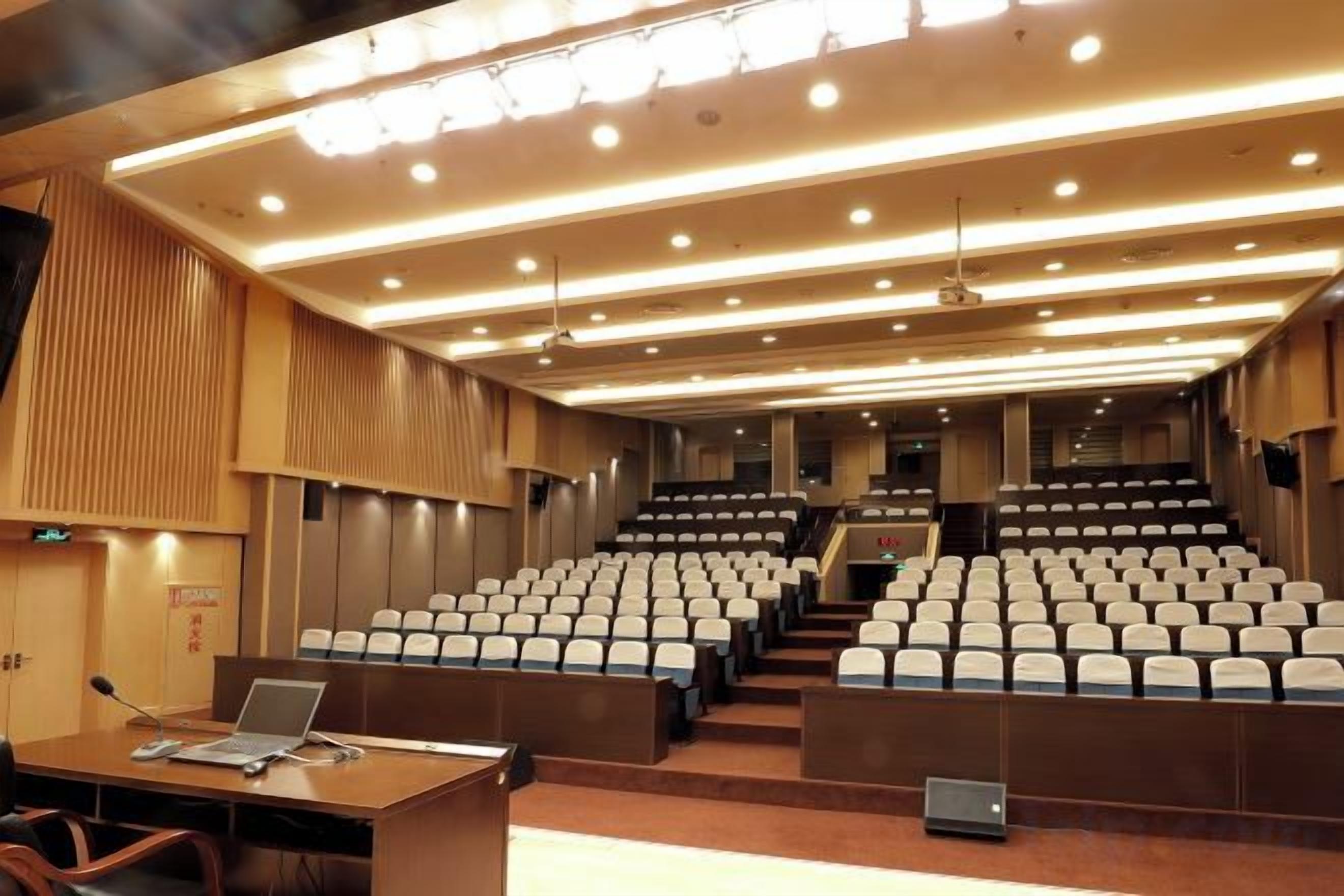 Sala de conferências com assentos em níveis, um púlpito e um laptop em uma mesa.