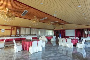 Uma sala de banquetes com mesas redondas, cadeiras brancas e lustres.