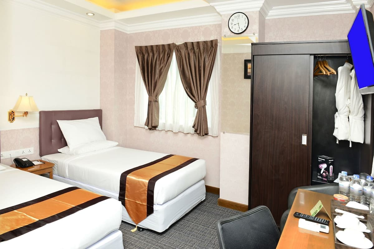 Quarto de hotel com duas camas, uma secretária com artigos de higiene, um guarda-roupa e um relógio na parede.